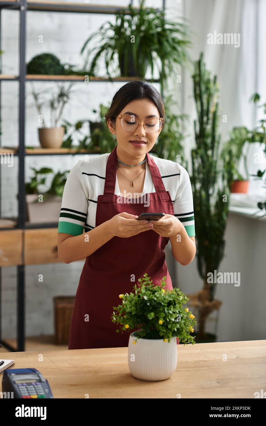 A young Asian woman, the owner of a plant store, checks her phone while ...