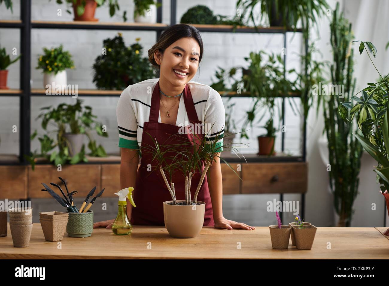 A young Asian woman, the owner of a plant shop, smiles brightly as she ...