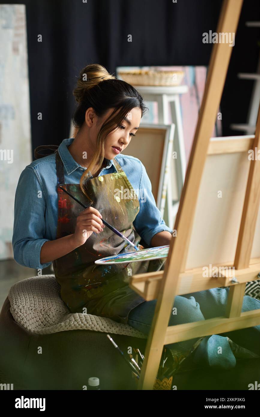 A young Asian artist paints in her workshop, focused on creating a ...