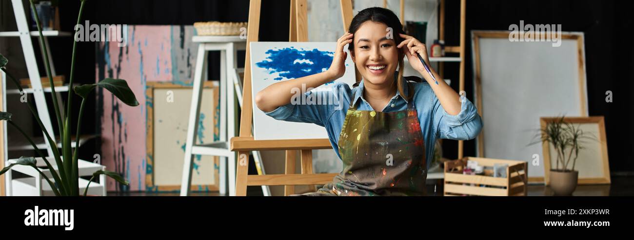 A young Asian artist, wearing an apron, smiles brightly as she takes a ...