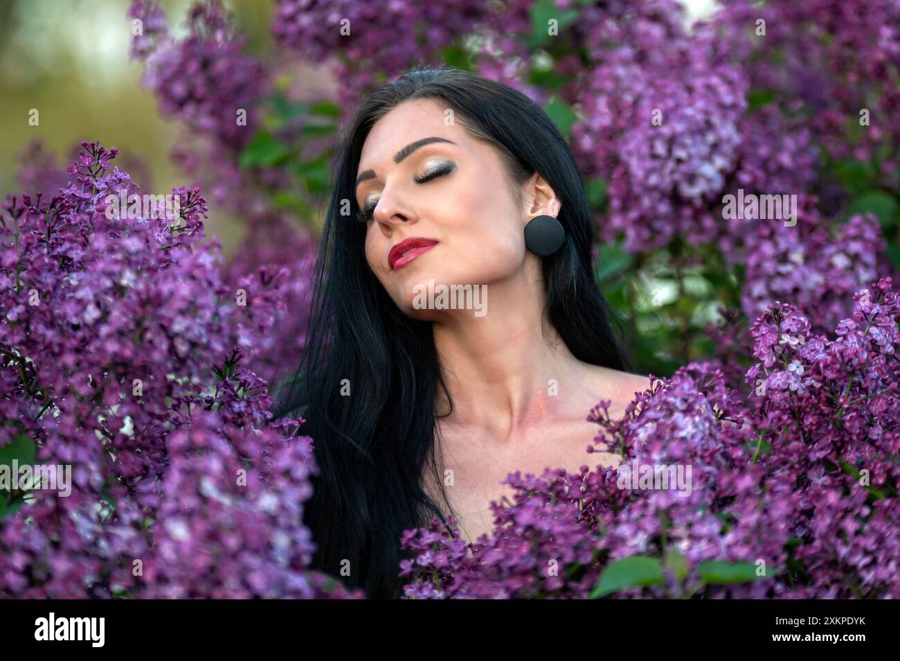 A woman with long black hair poses among purple lilac blossoms. Shallow ...