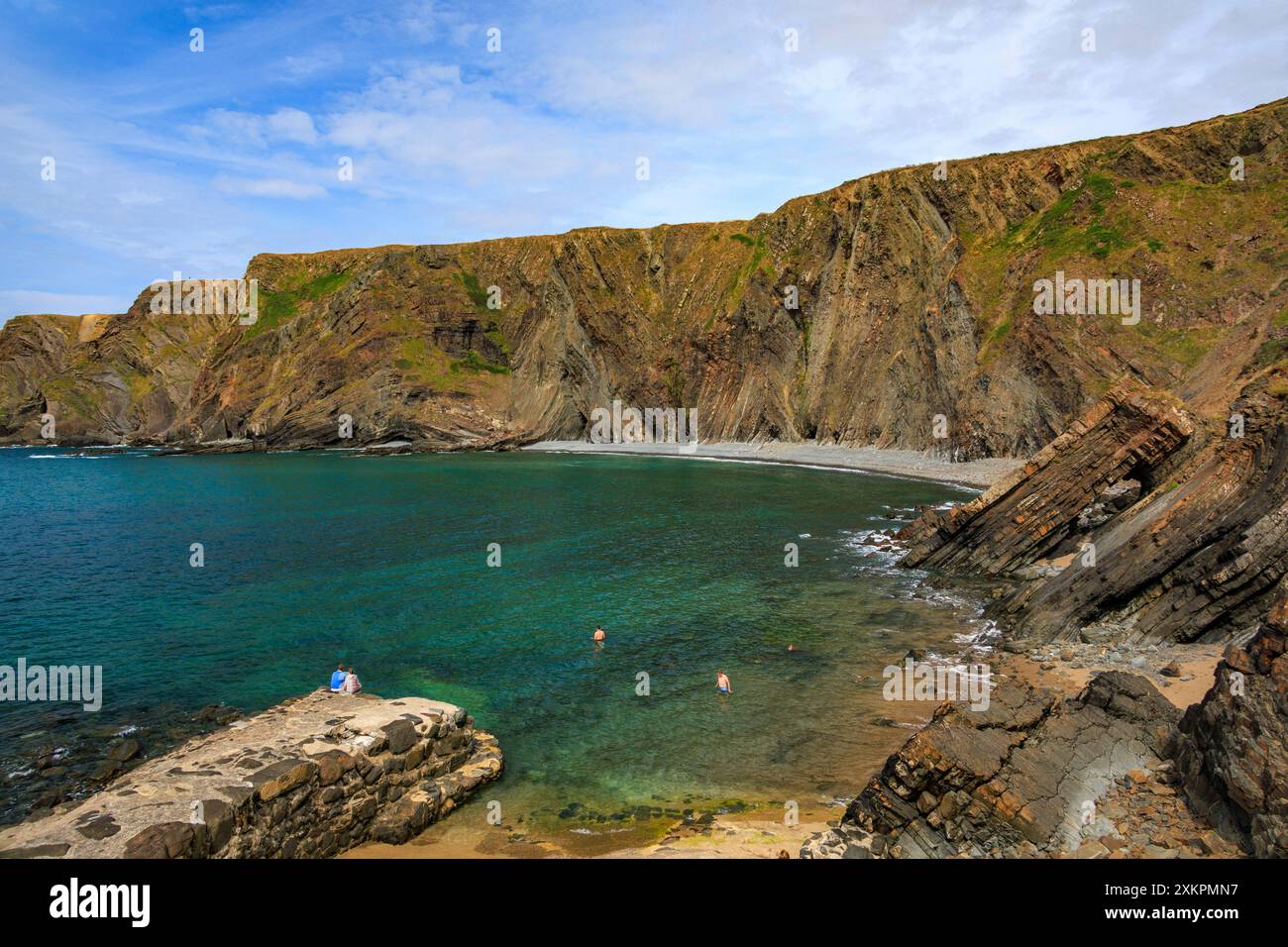 Swimmers in the bay under the dramatic folded rock strata of mudstones ...