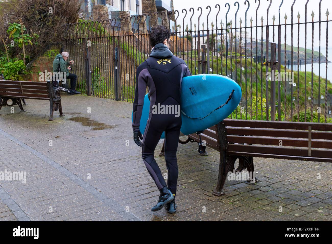 A surfer carrying his surfboard walking along a street in Newquay in ...