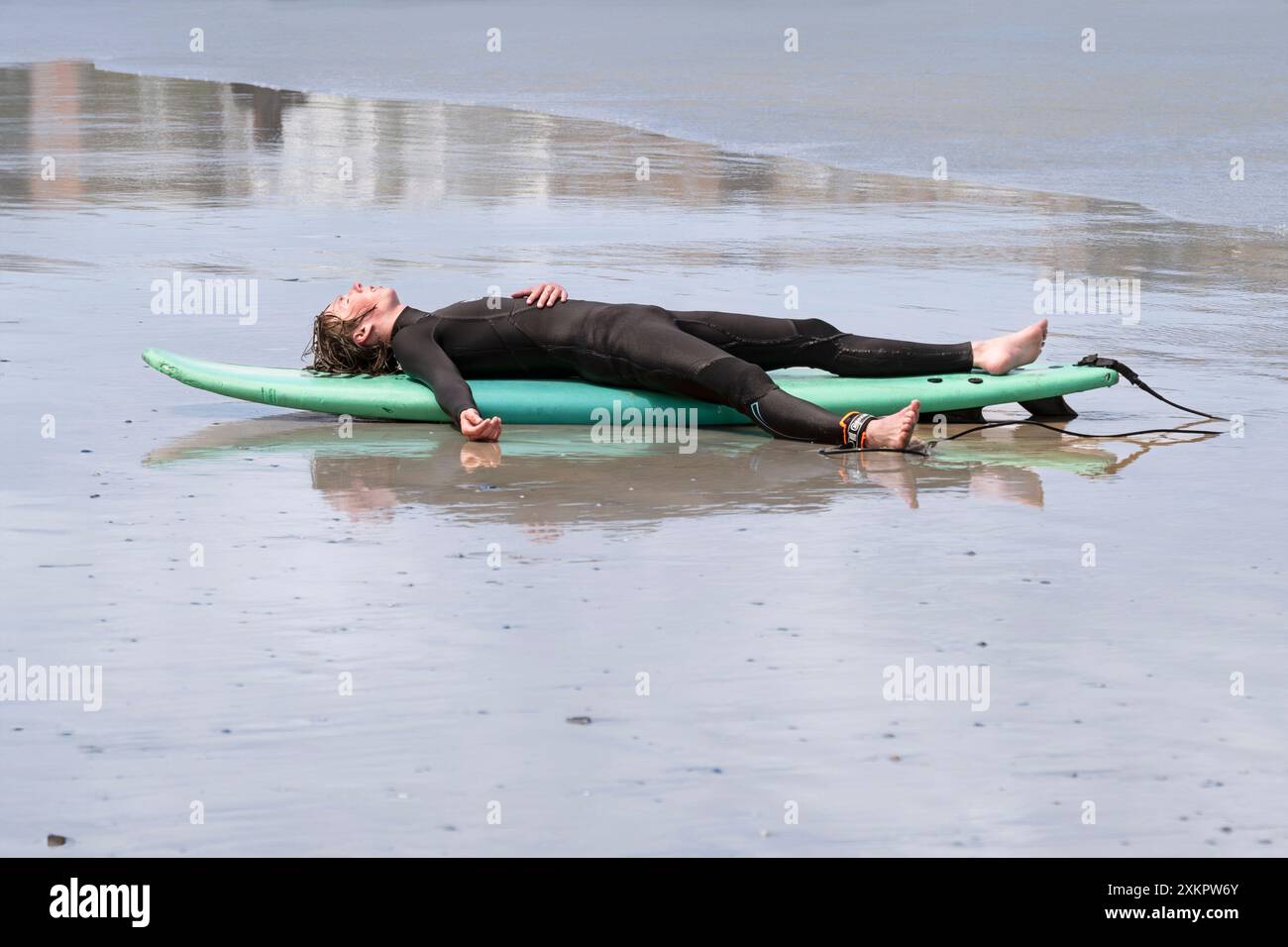 An exhausetd male surfer resting on his surfboard on the shoreline at ...