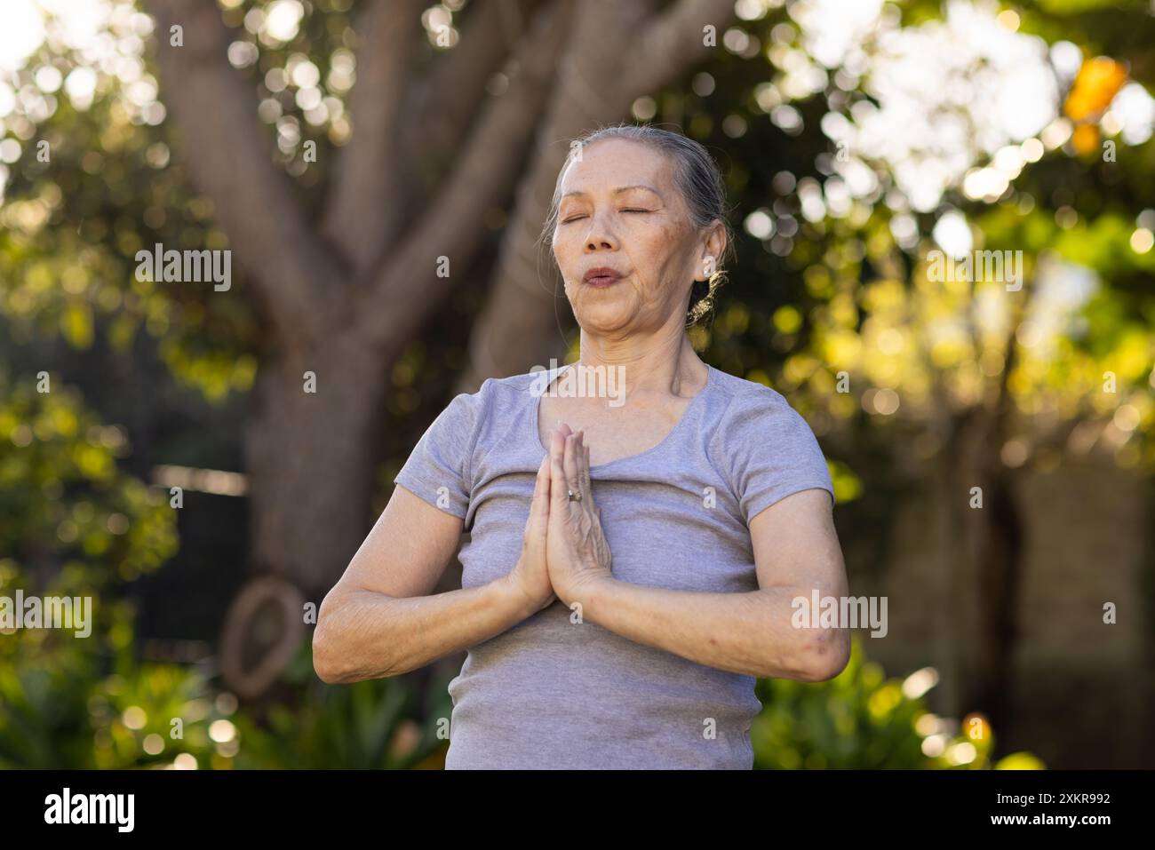 Practicing yoga, senior asian woman meditating outdoors with hands in ...