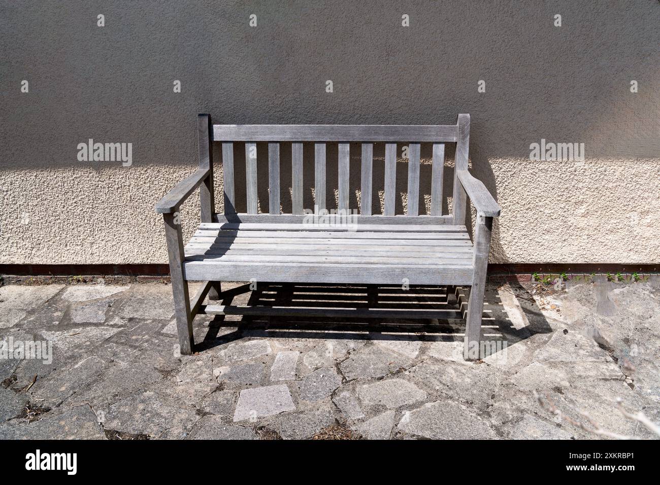 A wooden garden bench stands in the shade against a house wall. The ...