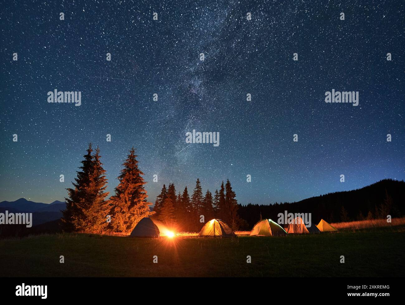 Night camping in mountains under starry sky. Tourist tents in campsite near burning campfire ...