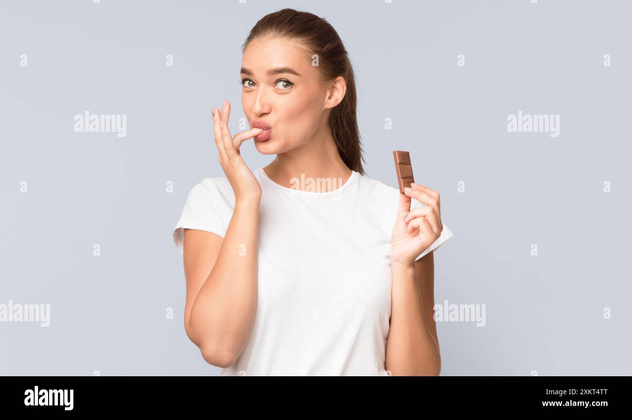 Millennial Girl Eating Chocolate And Licking Finger Standing On White ...