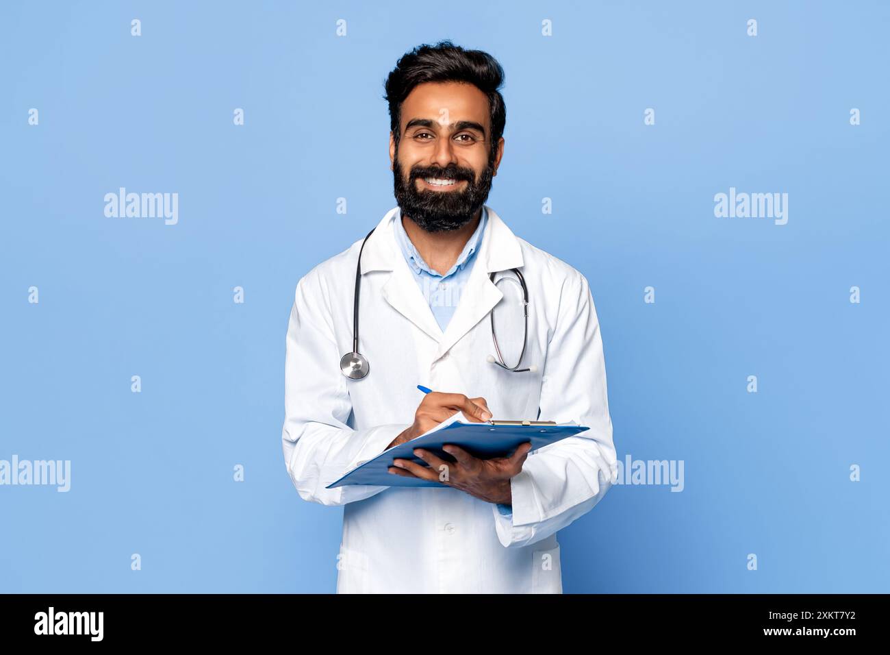 A smiling Indian man doctor with a beard is standing against a blue ...