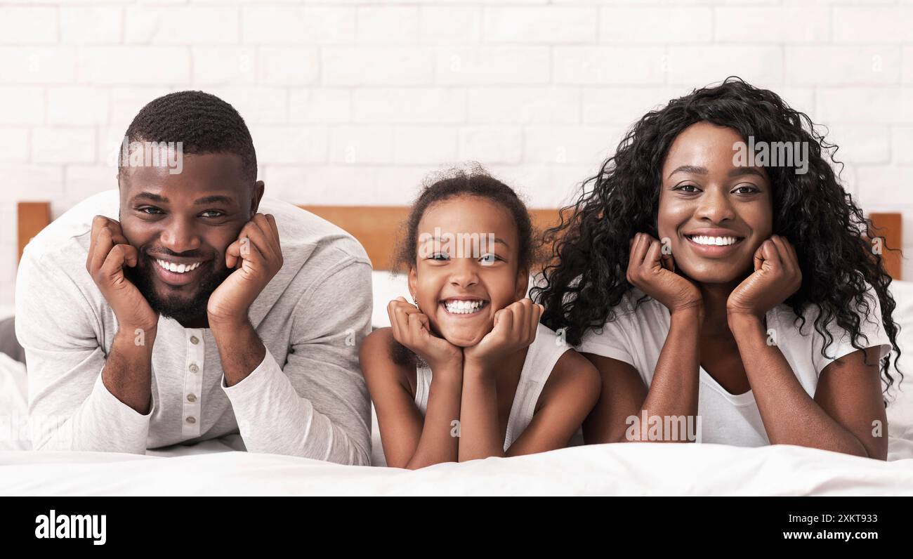 Portrait of happy black family lying on bed together, propping chin up ...