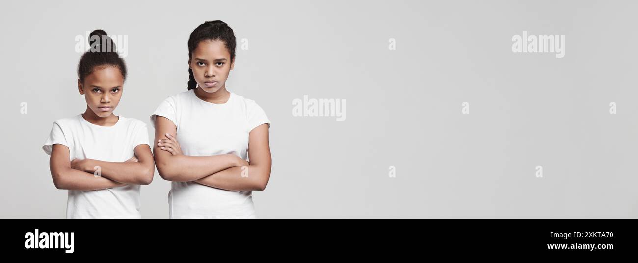 Mad african sisters staying next to each other with arms crossed ...