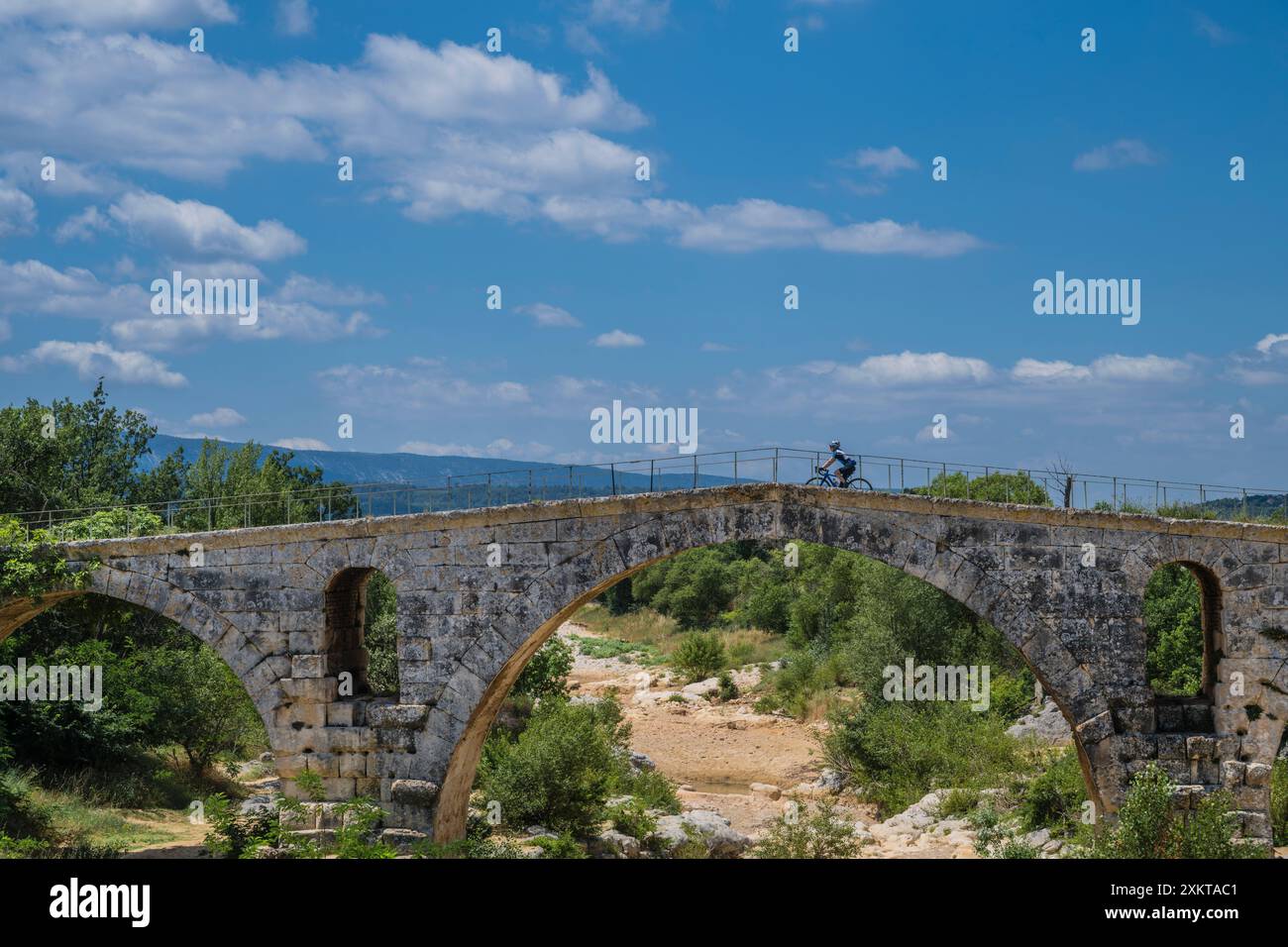 A male road cyclist riding over the 2000 year old Roman bridge, Pont ...