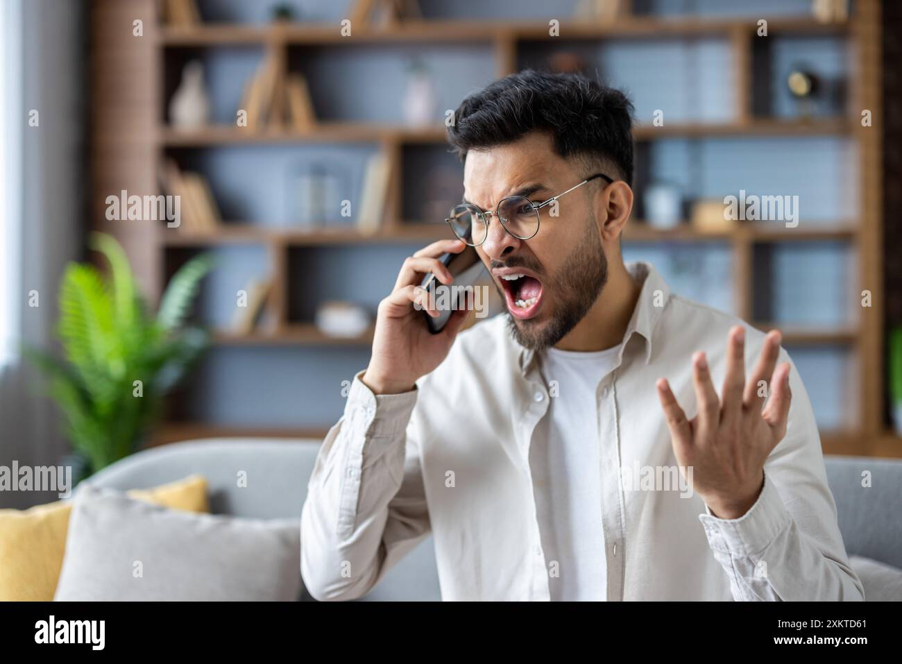 Angry man shouting on phone at home expressing frustration and stress ...