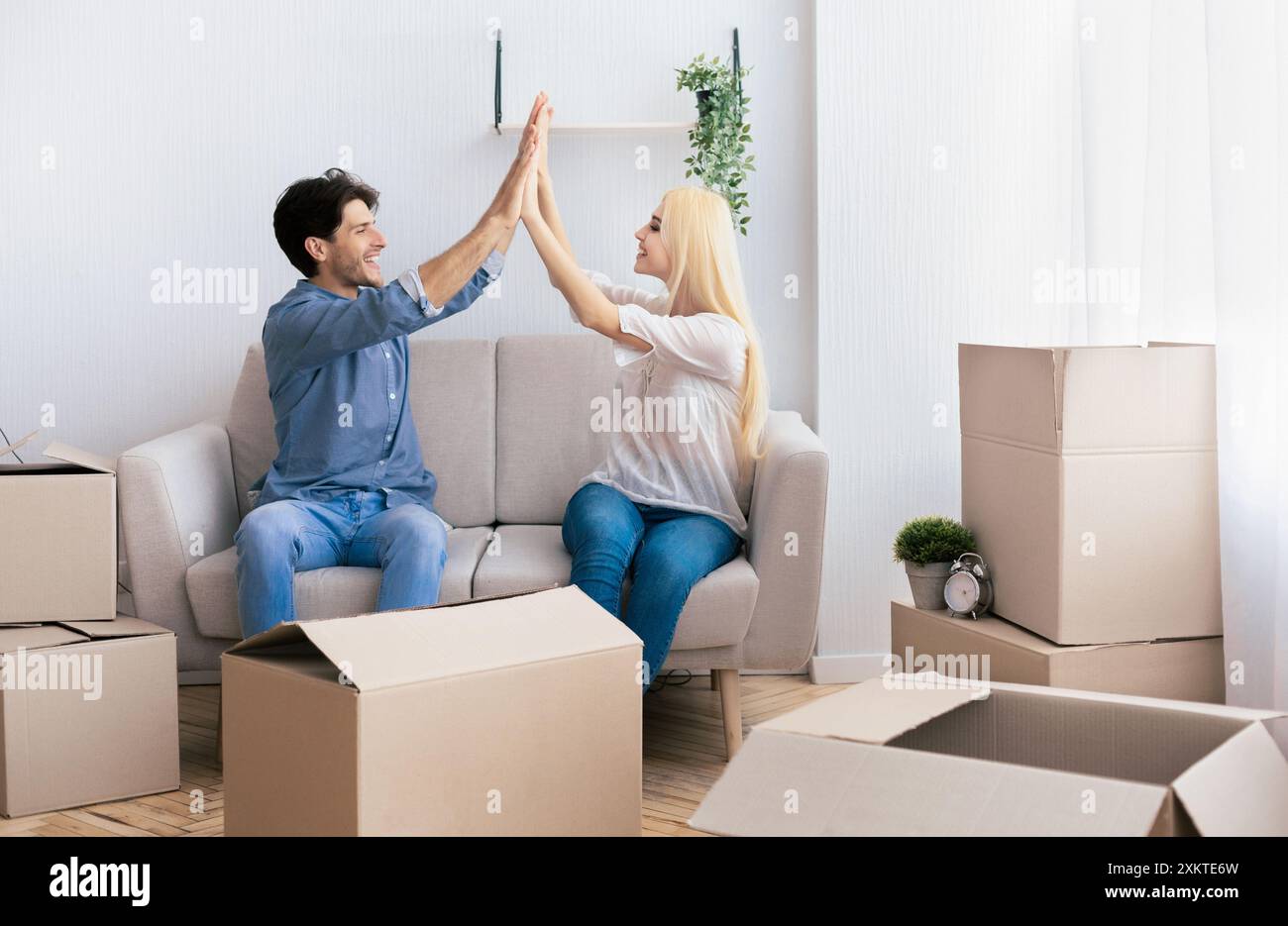 Successful Relocation. Young Couple Giving High-Five Sitting On Sofa Among Moving Boxes In New ...