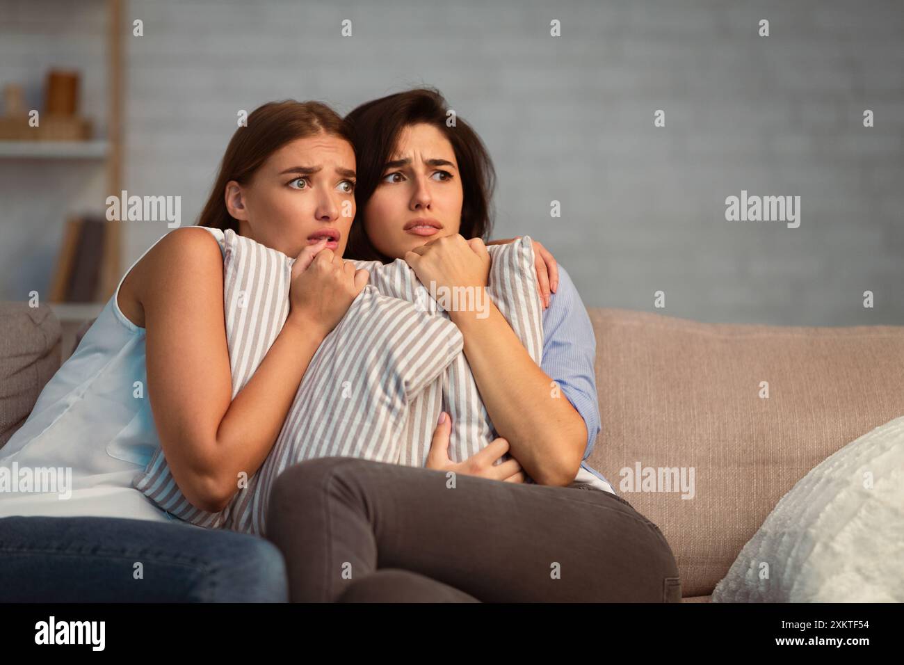 Two Scared Girls Hugging Pillows Sitting On Couch Alone At Home While ...