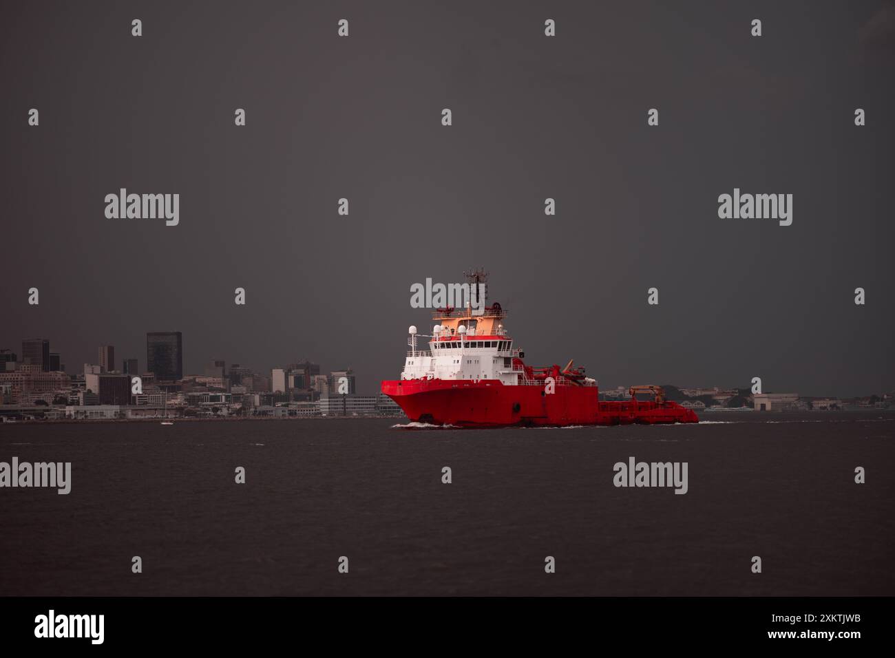 A red offshore support vessel sails on a dark, moody ocean with an ...