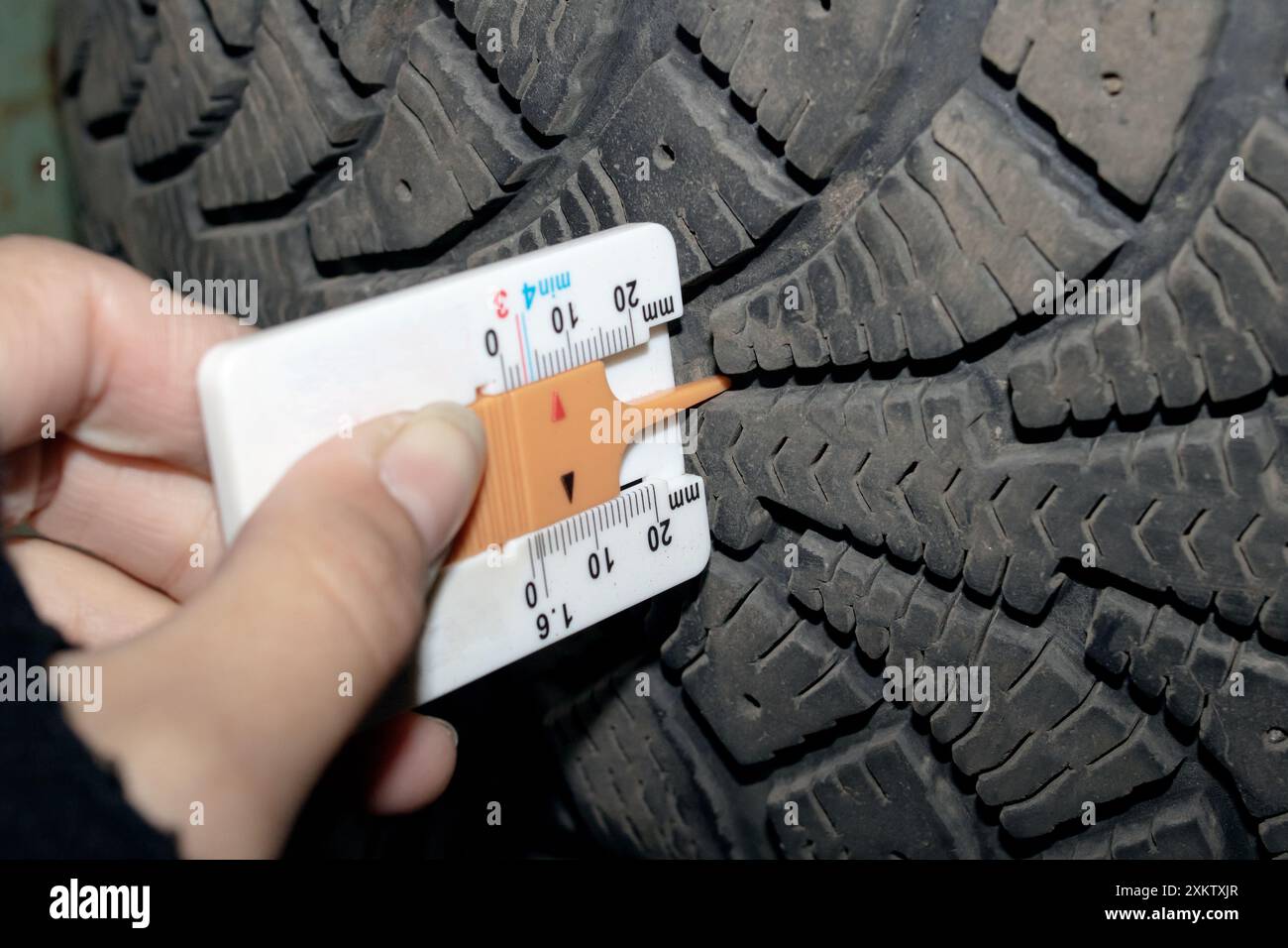 A person is using a ruler to measure the depth of a tire. The tire is ...