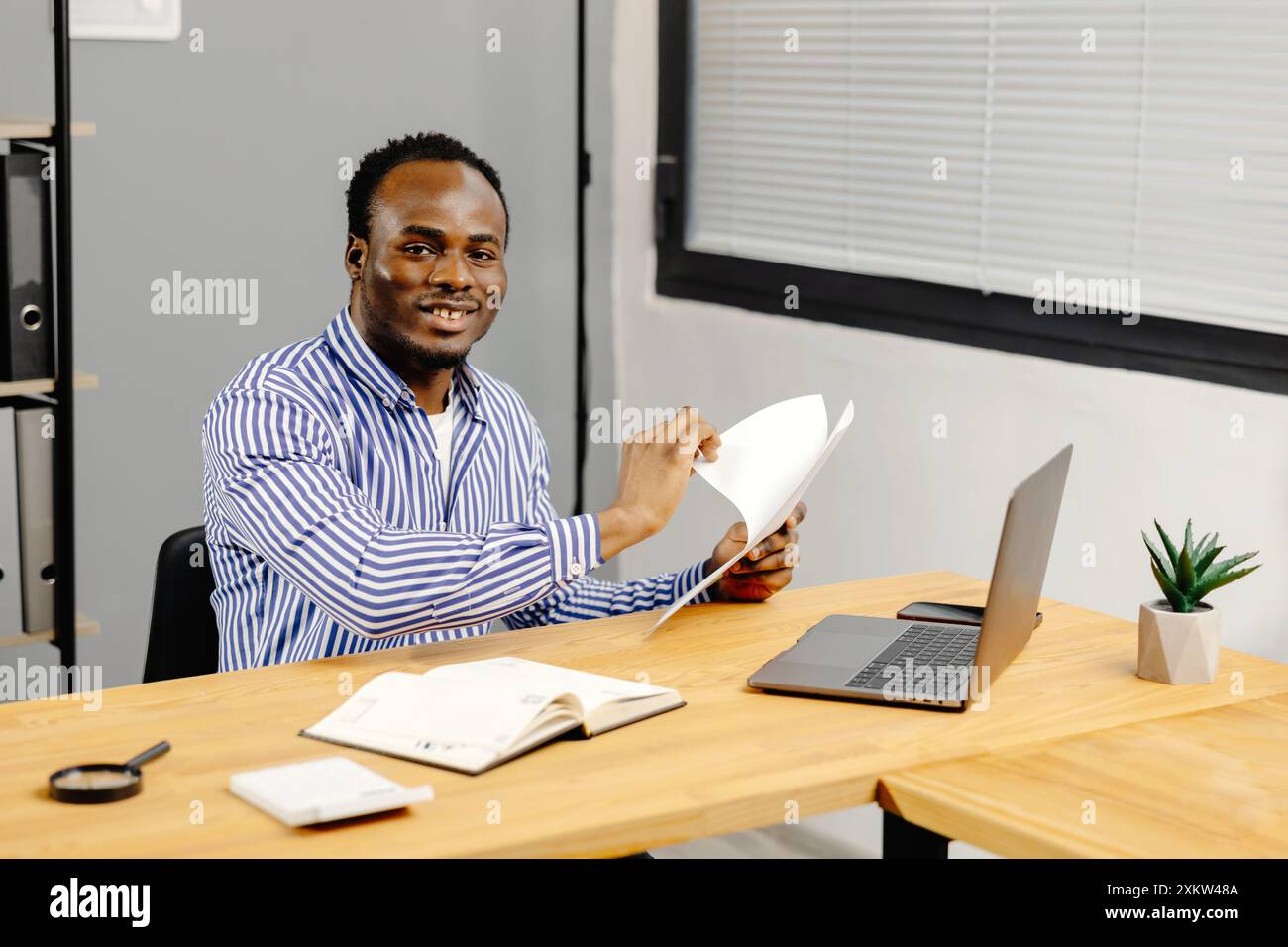 Man sitting at desk holding paper Stock Photo - Alamy