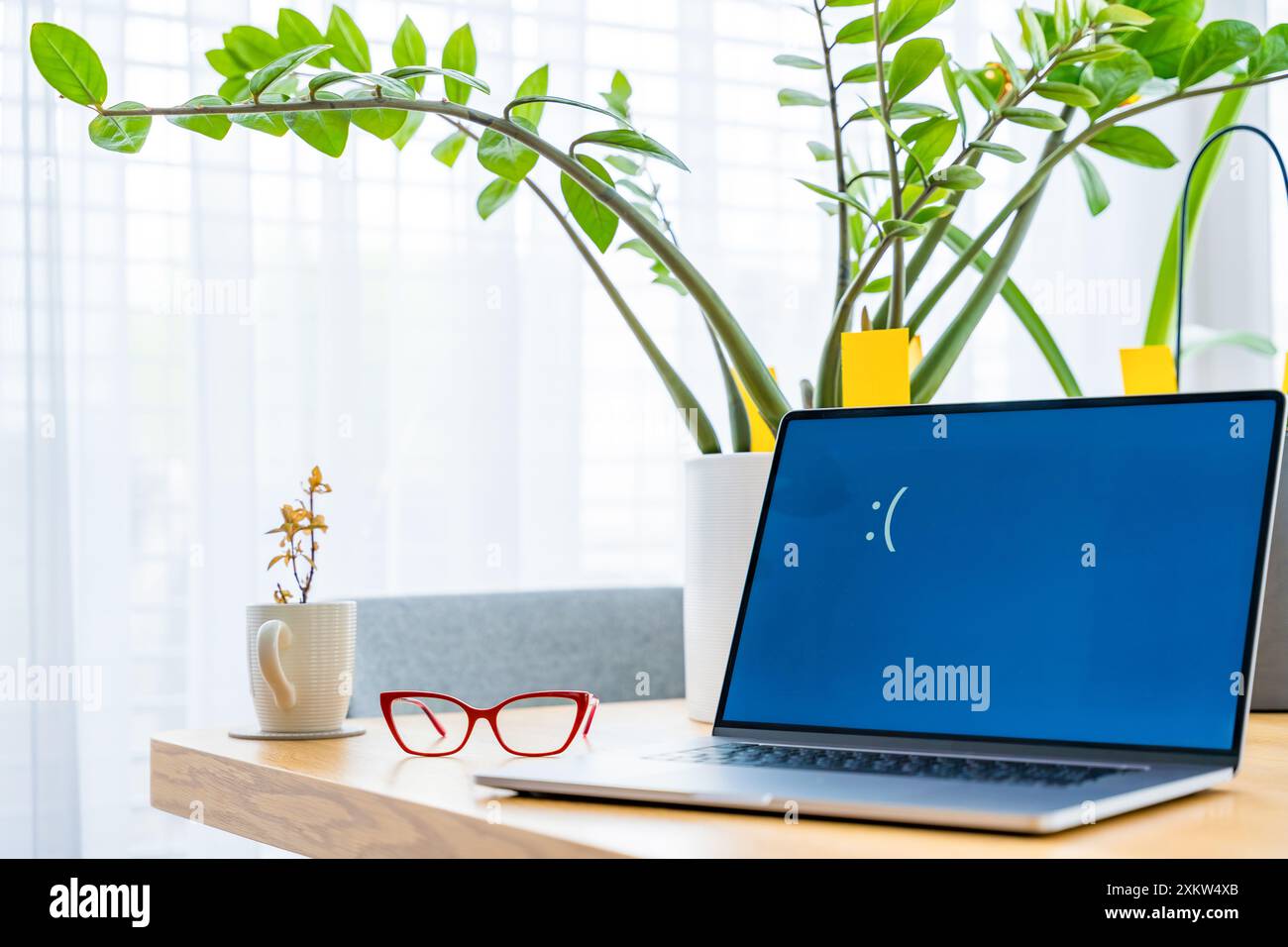 Sad laptop monitor with blue screen error on home office desk with ...