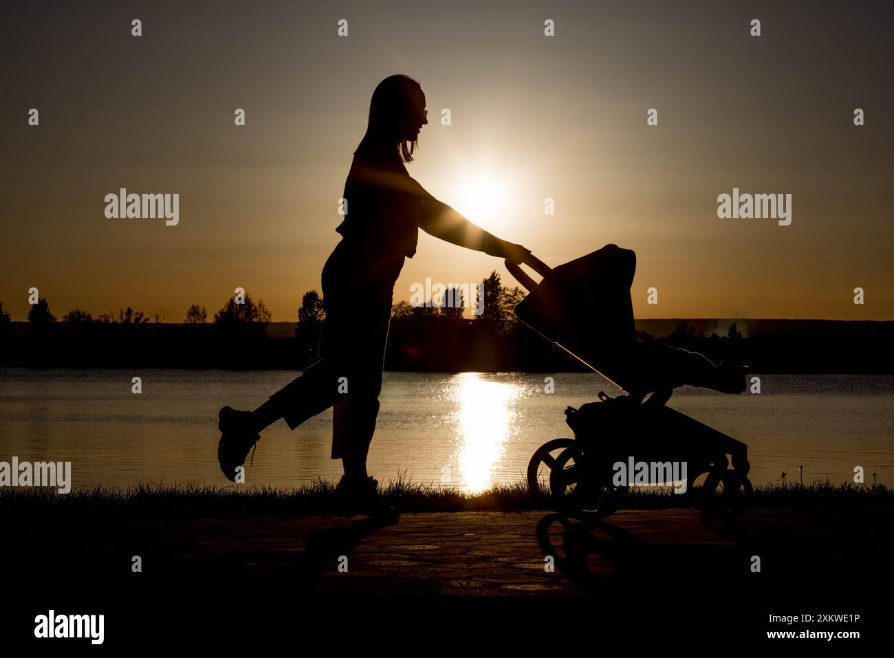 Silhouette of a mother pulling a baby carriage against the sunset near ...