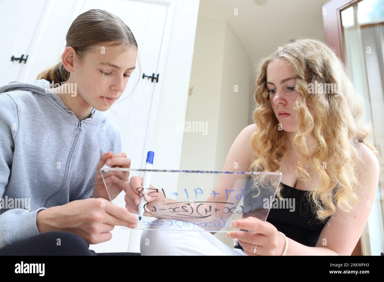 Two girls doing maths math sitting on floor writing on whiteboard with ...
