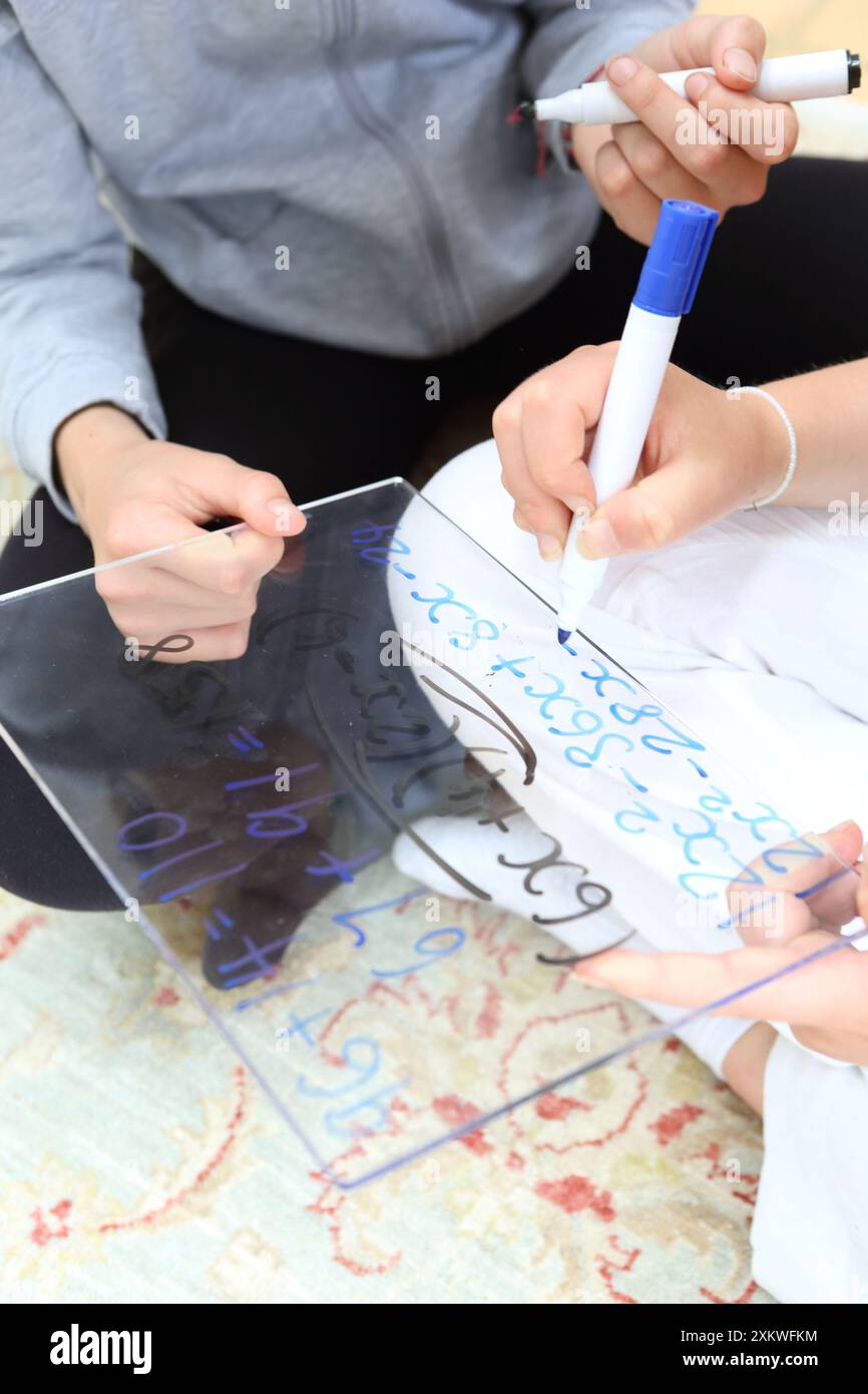 Girls doing maths math sitting on floor writing on whiteboard with pens ...
