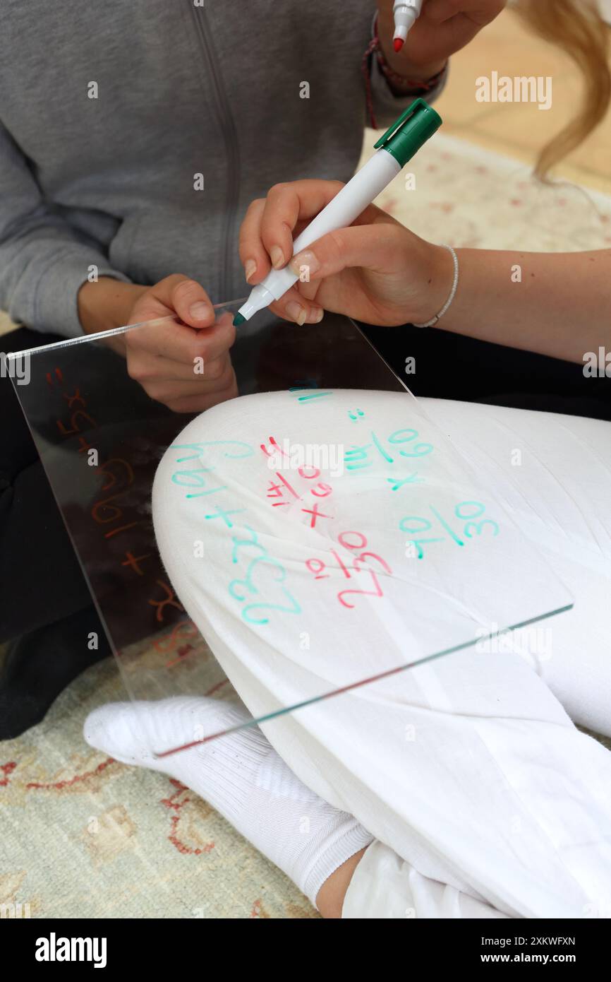 Girls doing maths math sitting on floor writing on whiteboard with pens ...