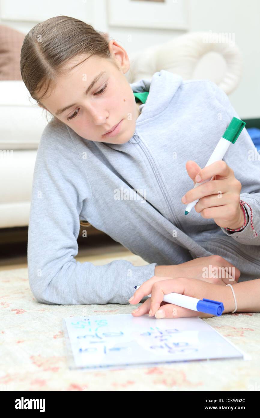 Girls doing maths math lying on floor writing on whiteboard with pens ...