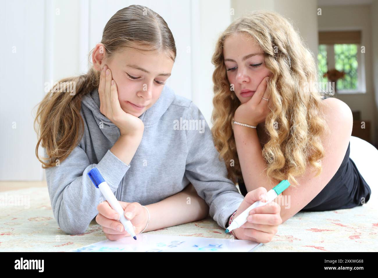 Two girls working lying on floor writing on whiteboard with pens ...