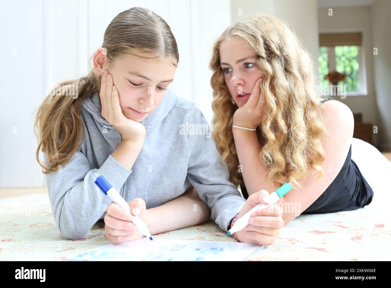 Two girls lying on floor writing on whiteboard with pens sisters ...