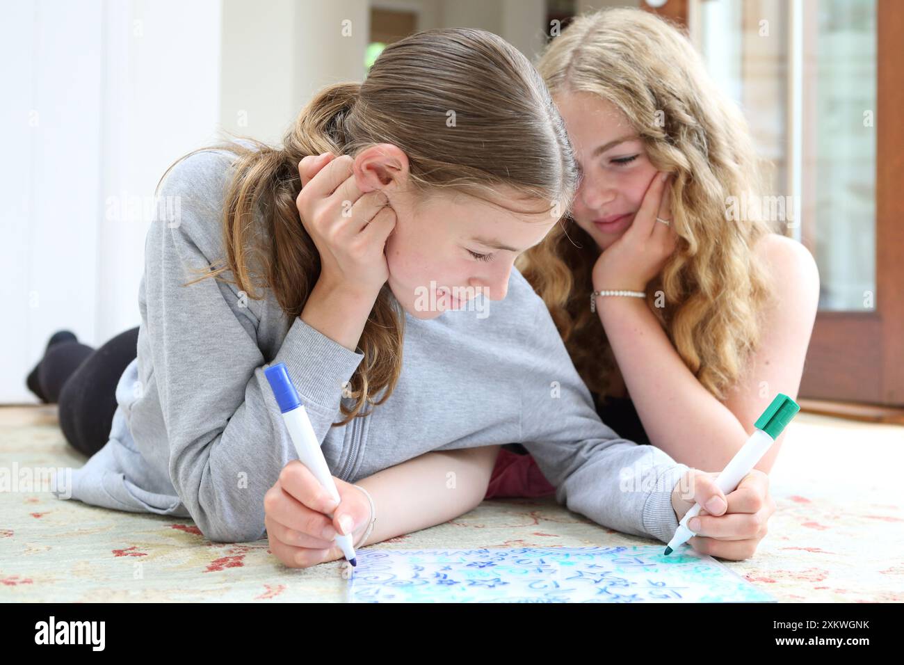 Two girls smiling doing maths math lying on floor writing on whiteboard ...