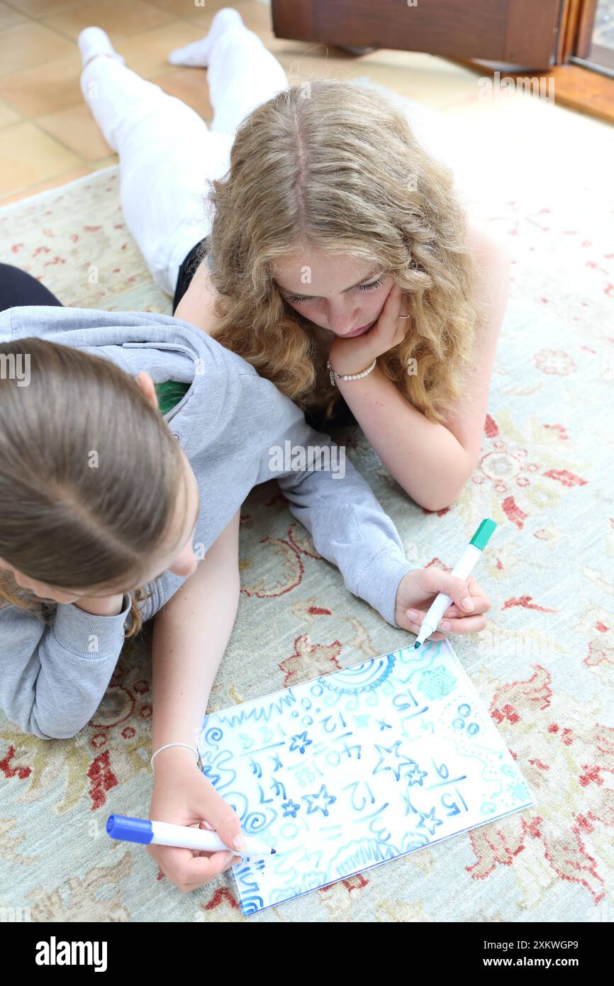 Two girls doing maths math lying on floor writing on whiteboard with ...