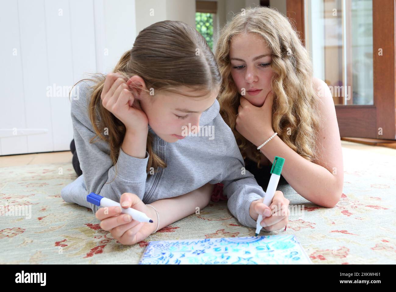 Two girls doing maths math lying on floor writing on whiteboard with ...