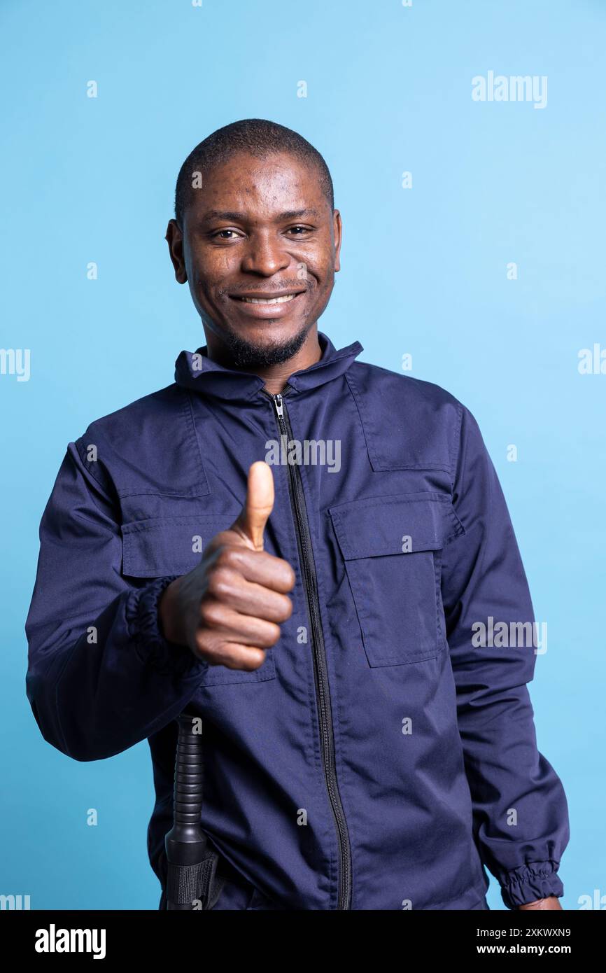 Positive security officer showing a thumbs up like symbol in studio, giving his approval on ...