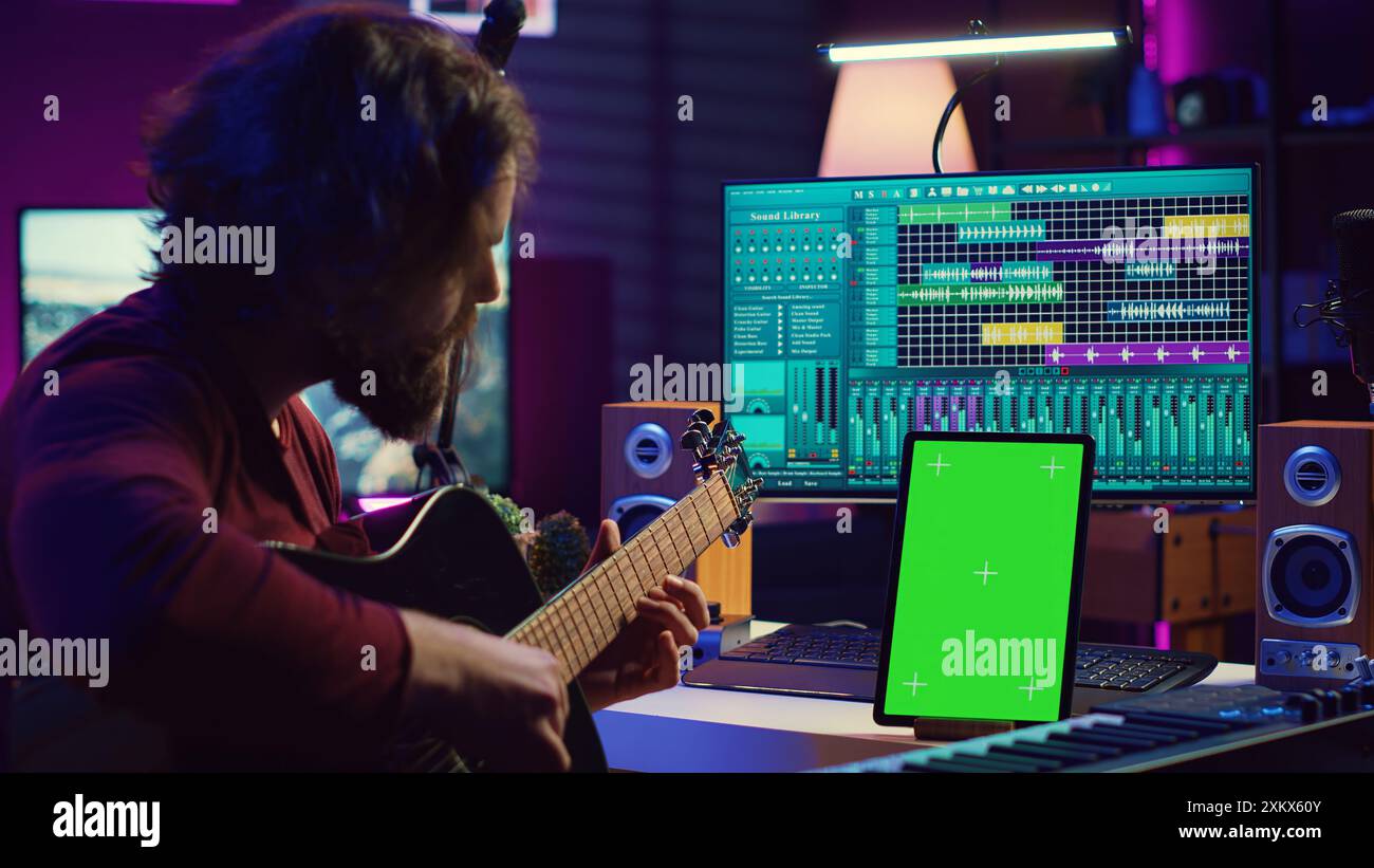 Sound engineer practices playing acoustic guitar using learning app tutorial on phone via ...