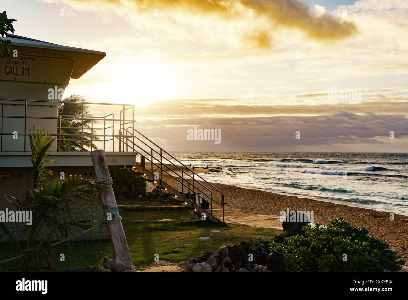 A lifeguard tower standing on a beach with the sun setting in the ...