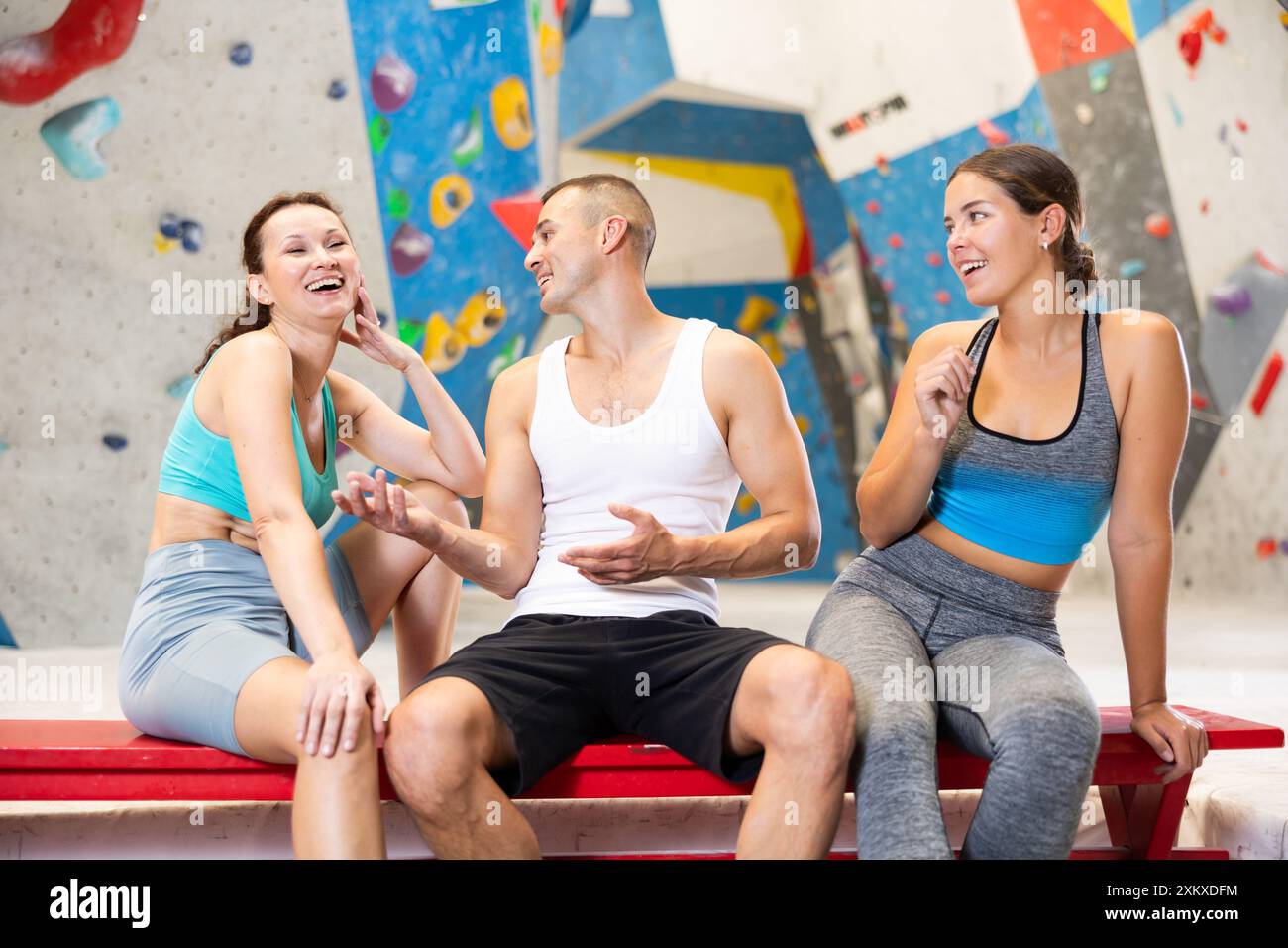 Three friends, man and woman, discuss their climbs on climbing wall ...