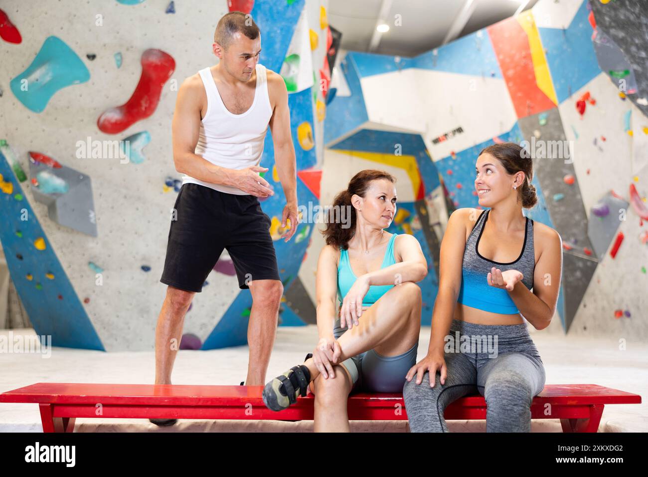 Three friends, man and woman, discuss their climbs on climbing wall ...