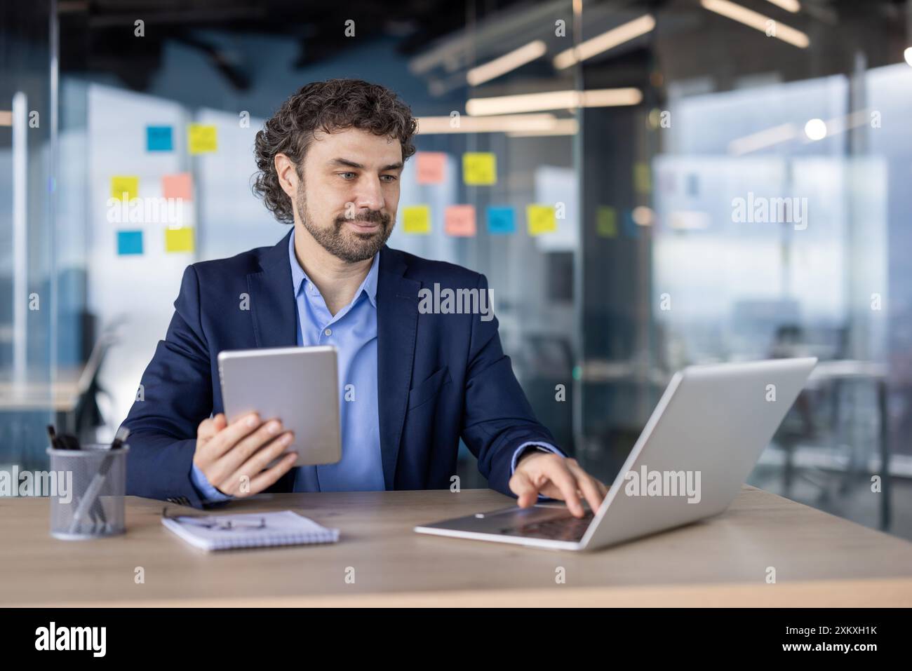 Businessman in formal attire working on laptop and holding tablet in ...