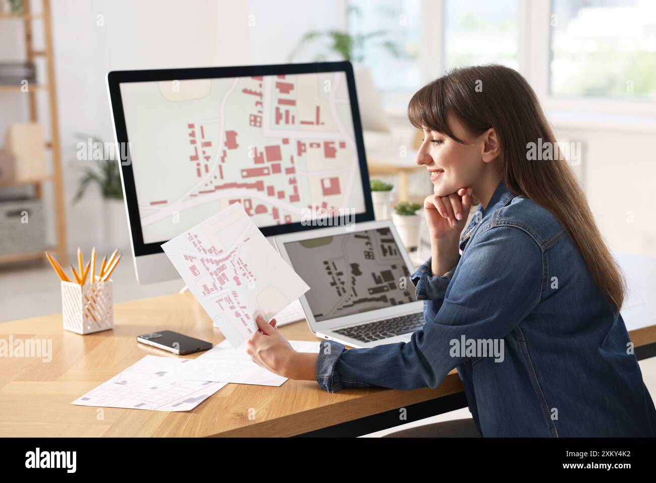 Smiling cartographer working with cadastral maps at table in office ...