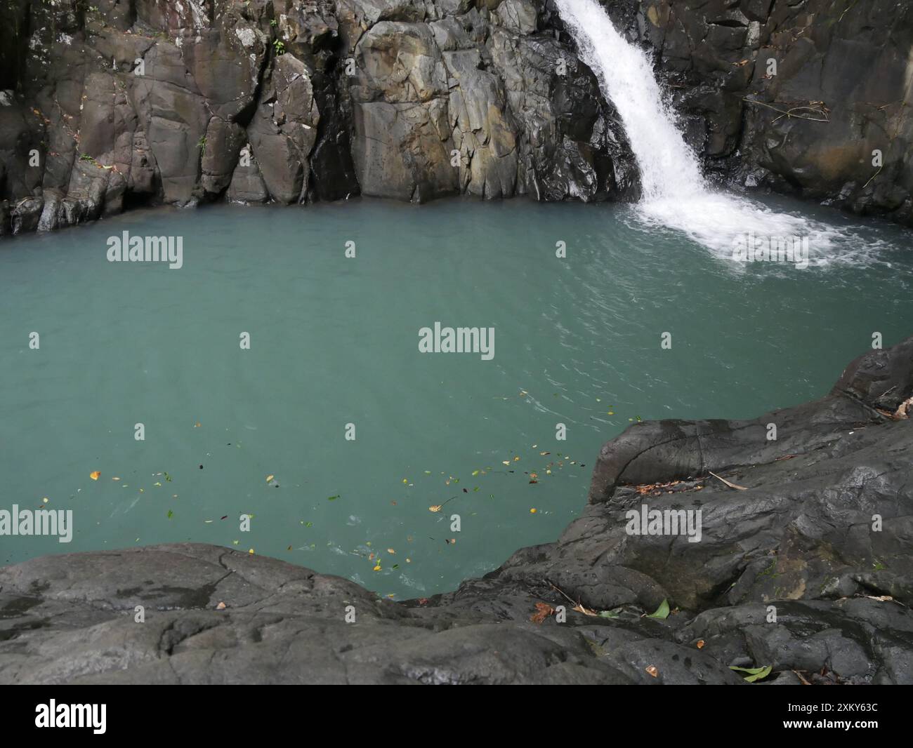 A picturesque waterfall cascades over rocks into a tranquil pool of ...