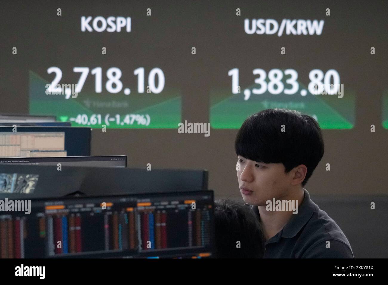 A currency trader watches monitors near the screen showing the Korea Composite Stock Price Index ...