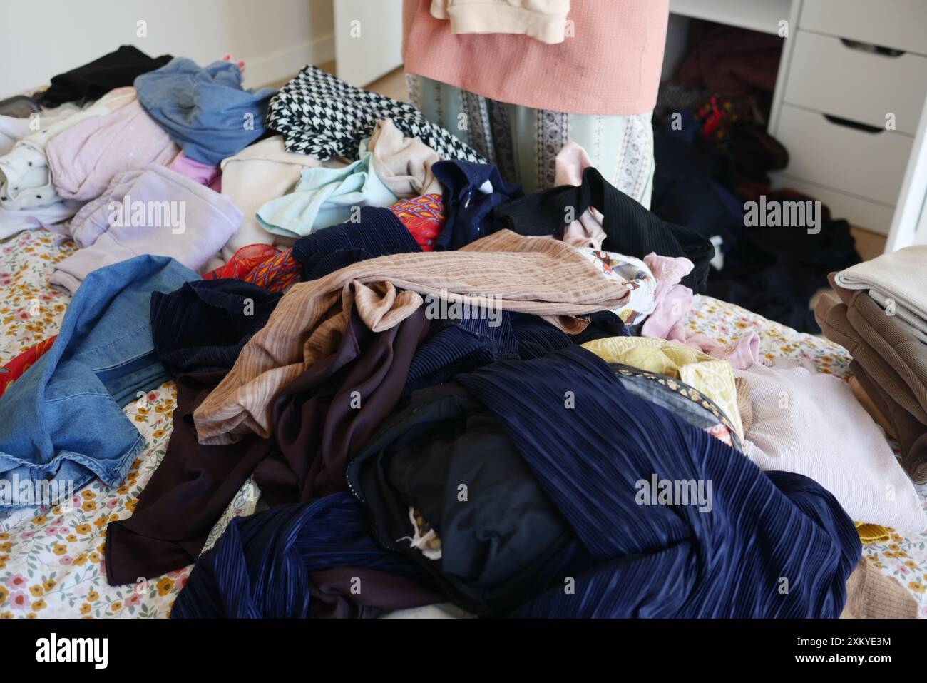 The bedroom is in a chaotic state, with clothes strewn across the bed ...