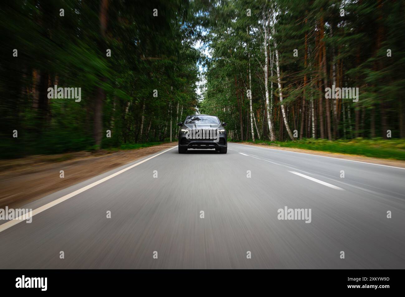 A gray new SUV is driving along a highway in the forest with a blurred ...