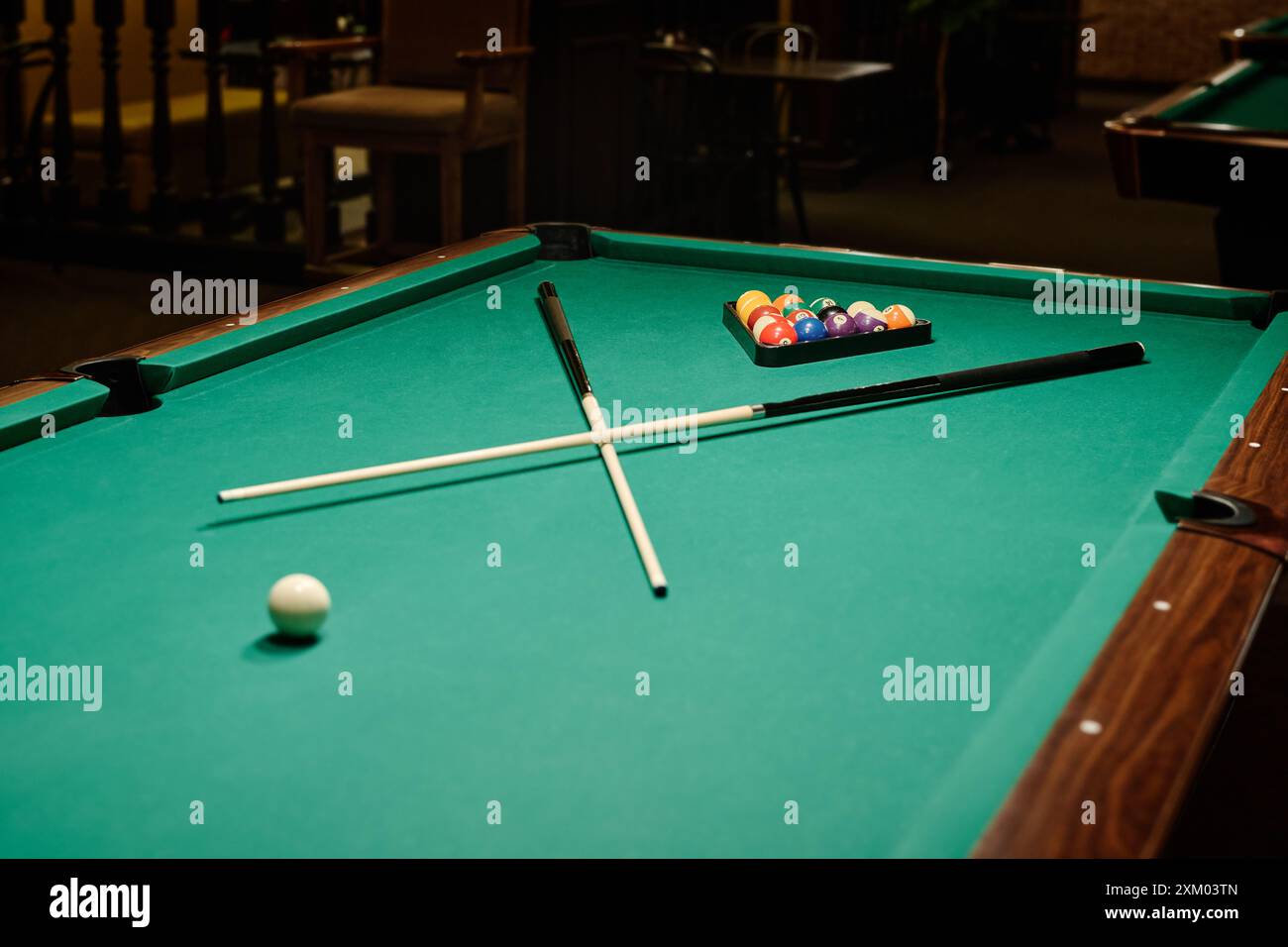 Wide and long table with green top and two crossed billiard cues lying ...