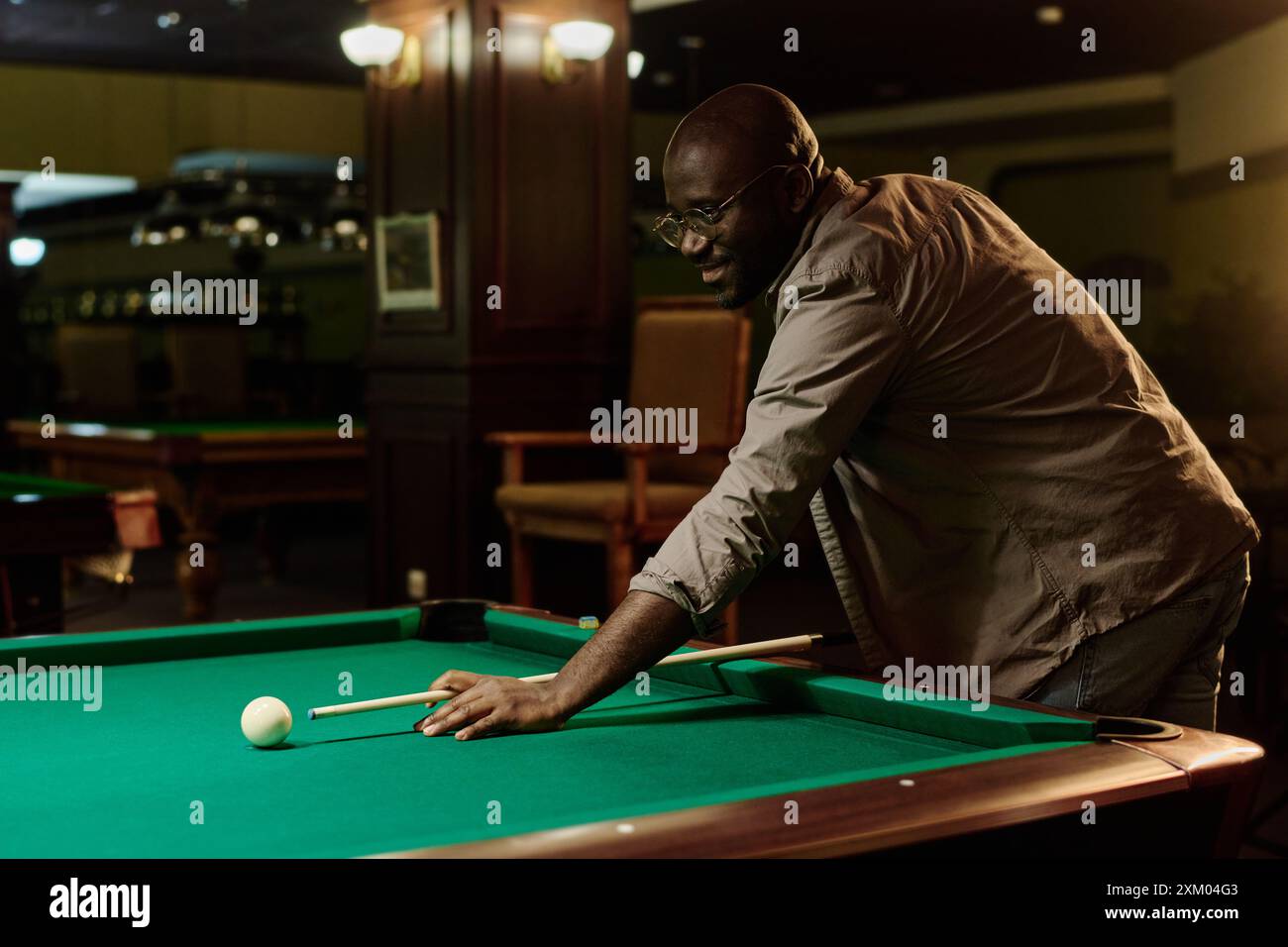 Happy young African American man with cue bending over green table and ...