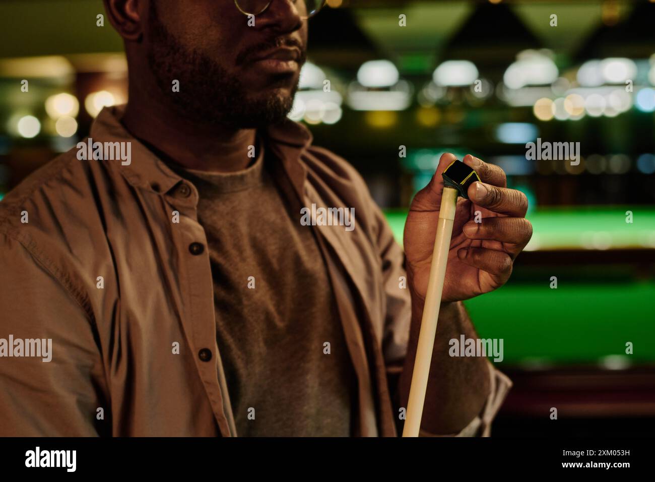 Hand of young African American male pool player rubbing tip of billiard ...