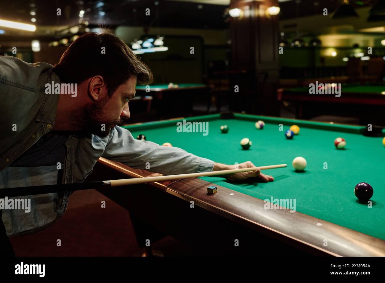 Side view of young male pool player in denim shirt or jacket bending ...
