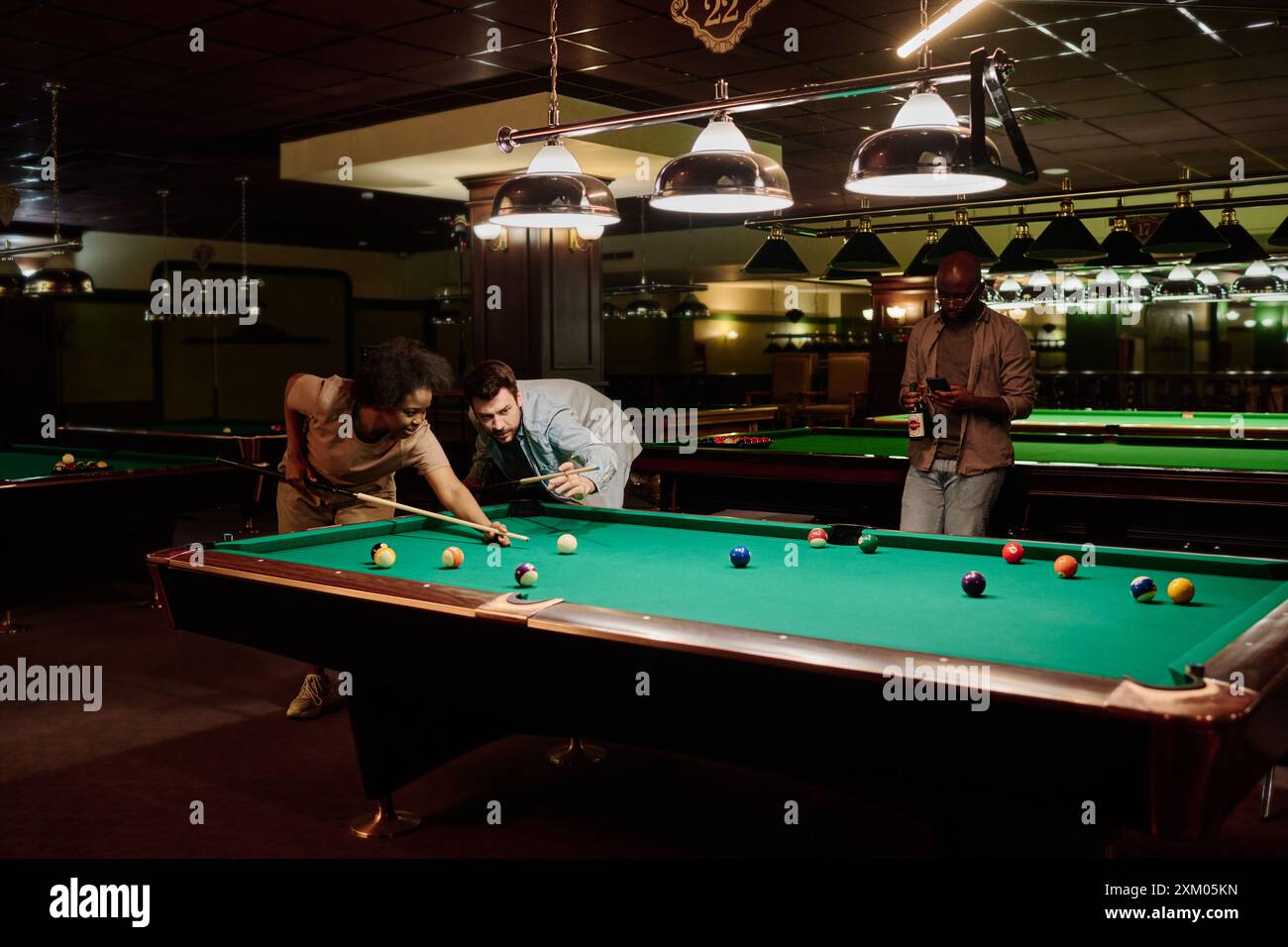Young man bending over wide pool table while standing next to his ...