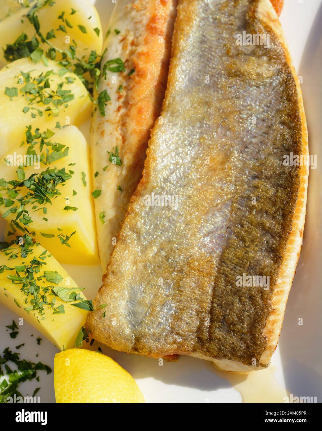 A piece of fried fish fillet with boiled potatoes on a plate in ...